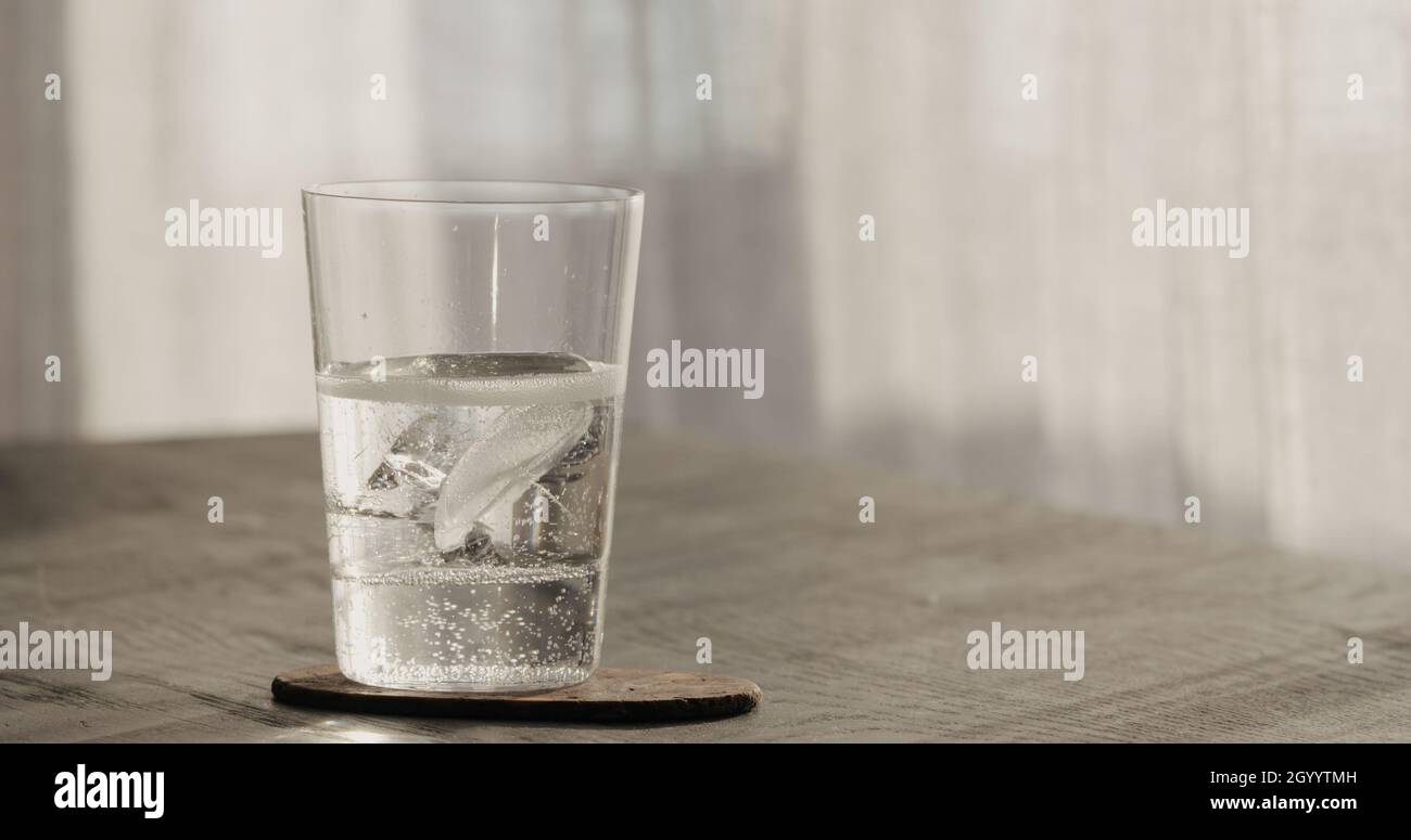 clear ice cube in tumbler glass with tonic on black oak table, wide ...