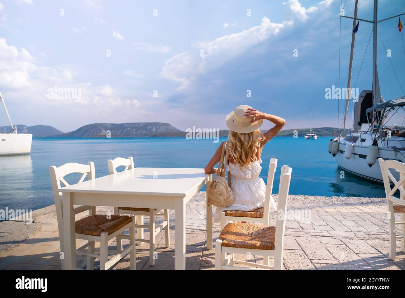 Young woman tourist in straw hat sitting at cafe at Ermioni marina ...
