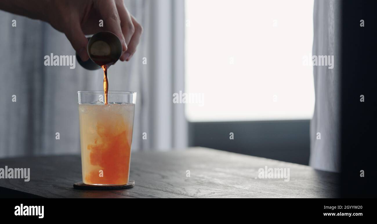 pour orange syrup into lemonade with crushed ice in tumbler glass on ...