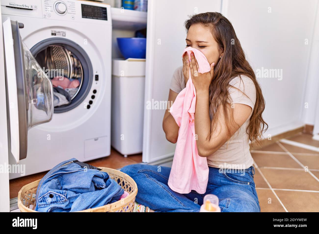 Young hispanic girl doing laundry smelling clean clothes at home Stock ...