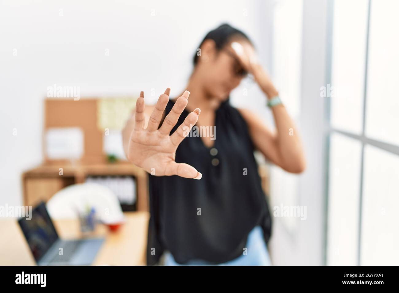 Young hispanic business woman working at the office covering eyes with ...
