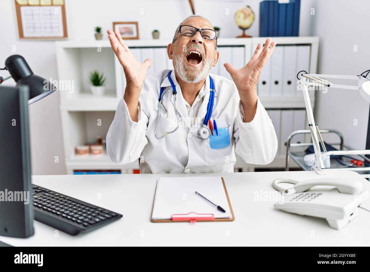 Mature doctor man at the clinic crazy and mad shouting and yelling with ...