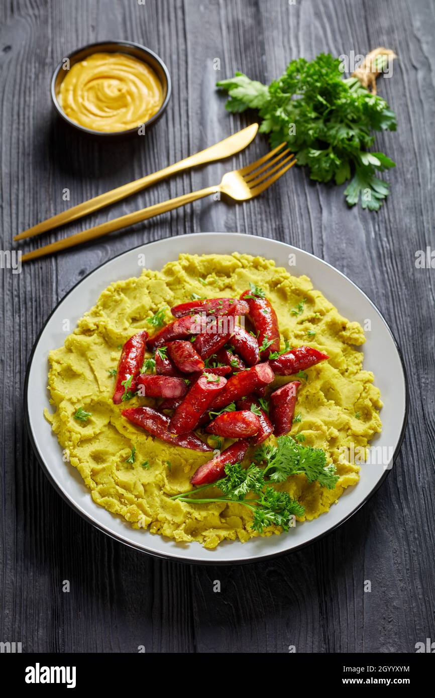 mashed green peas with fried deviled sausages on black plate on a ...