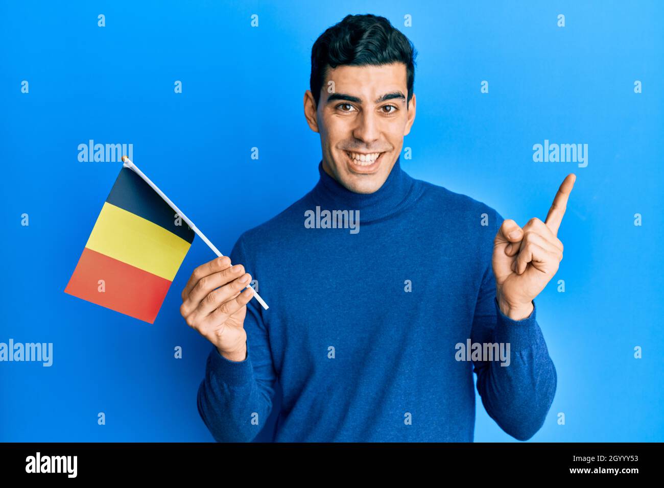 Handsome hispanic man holding belgium flag smiling happy pointing with ...