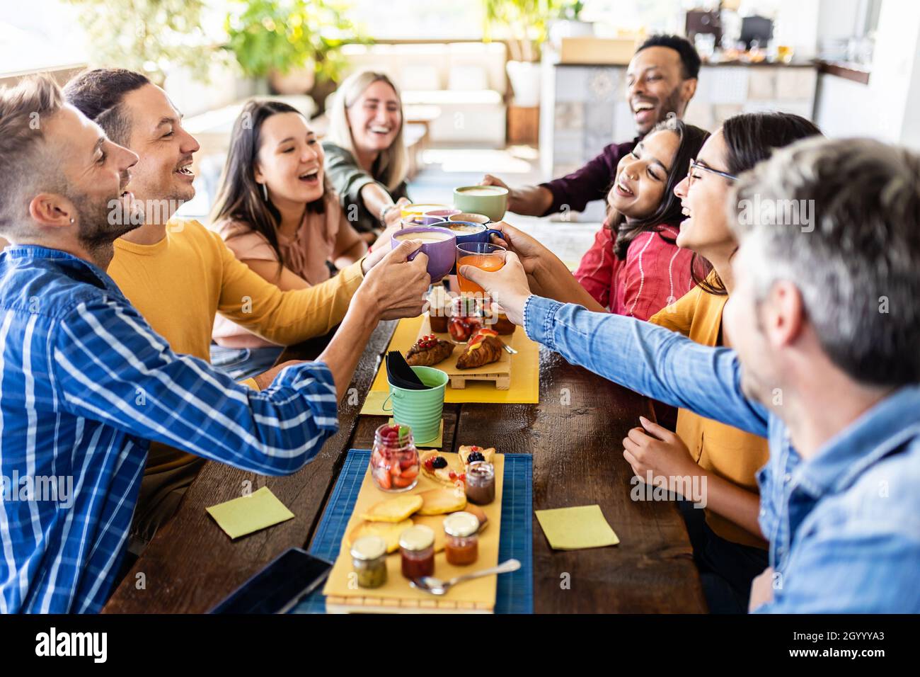 Smiling multiracial group of young people having breakfast and laughing ...