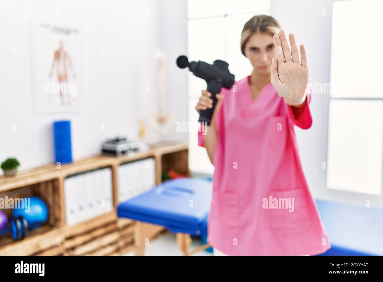 Young physiotherapist woman holding therapy massage gun at wellness ...