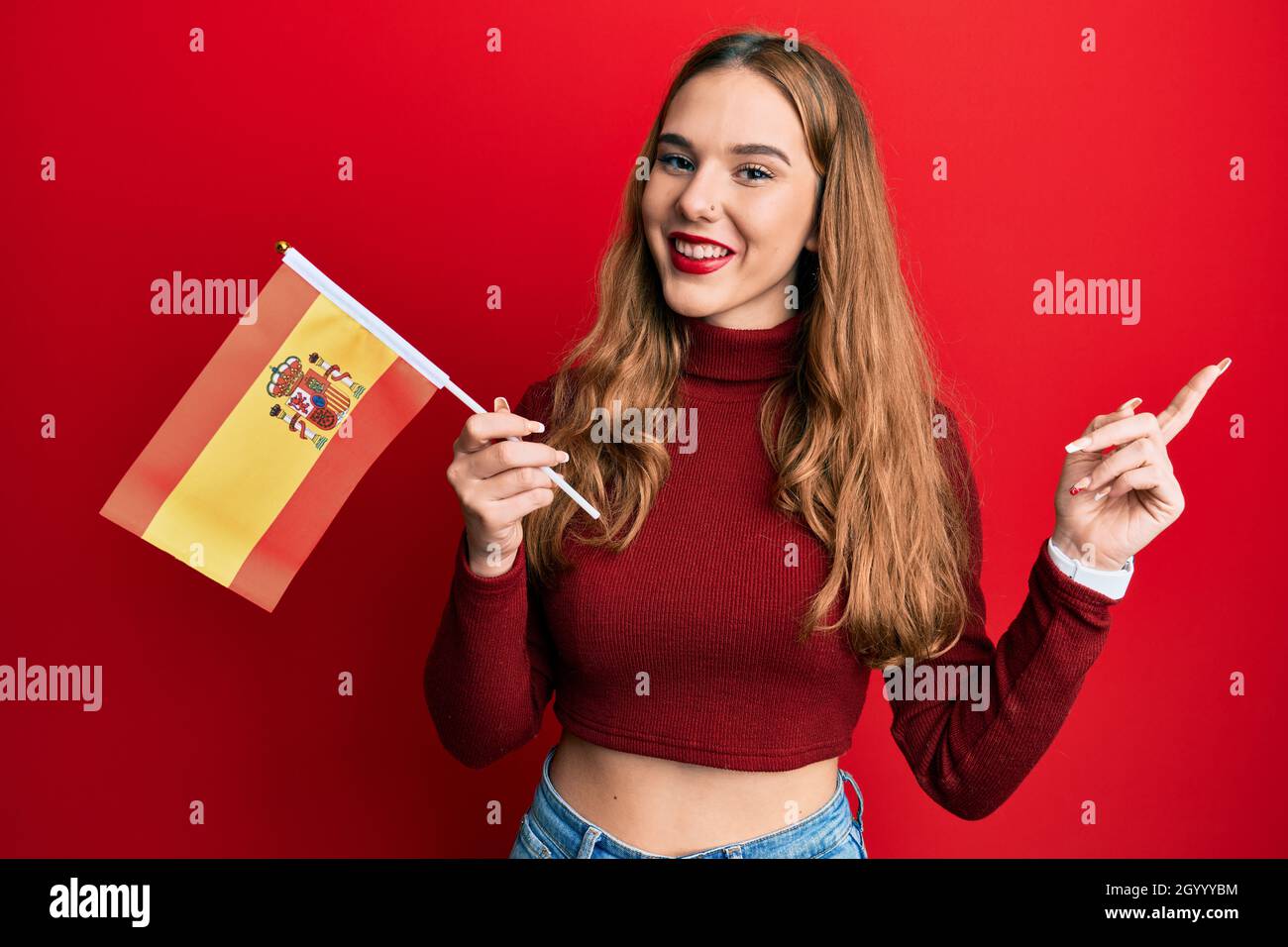 Young blonde woman holding spain flag smiling happy pointing with hand ...