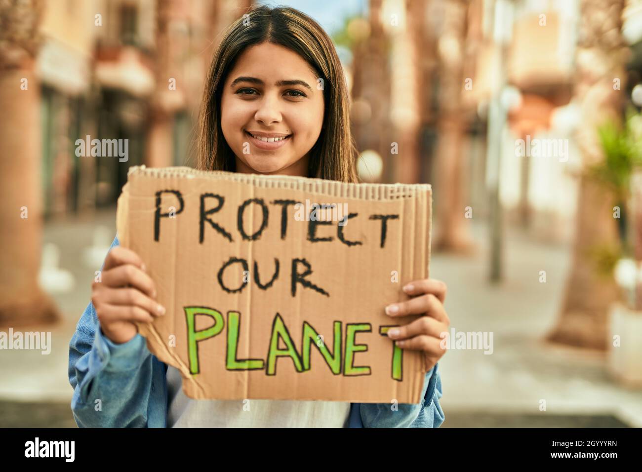 Young latin girl smiling happy holding protect our planet banner at the ...