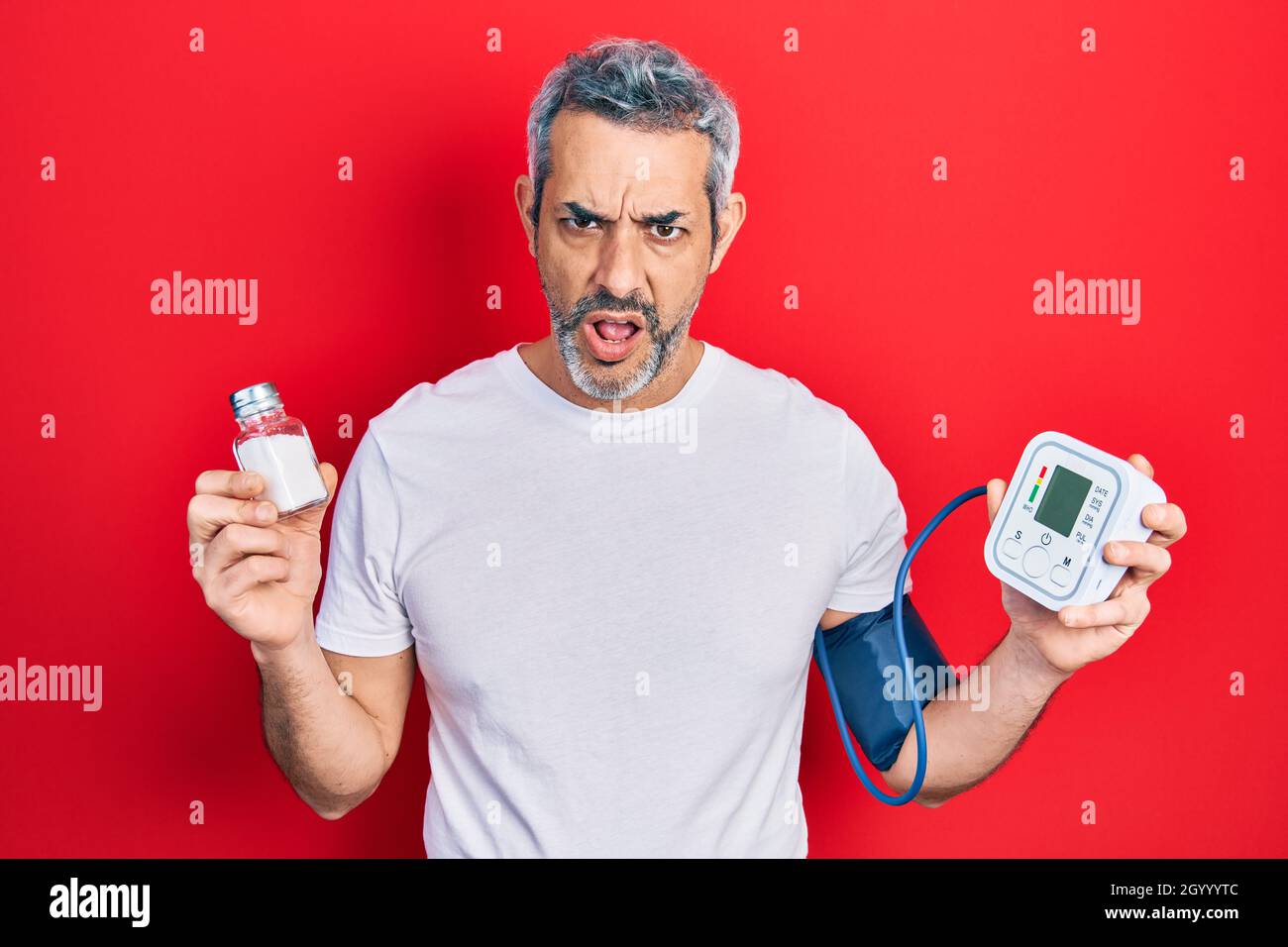 Handsome middle age man with grey hair using blood pressure monitor ...
