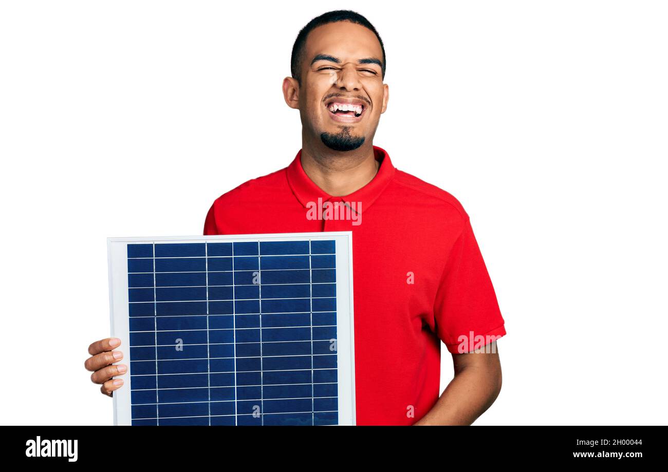 Young african american man holding photovoltaic solar panel celebrating ...