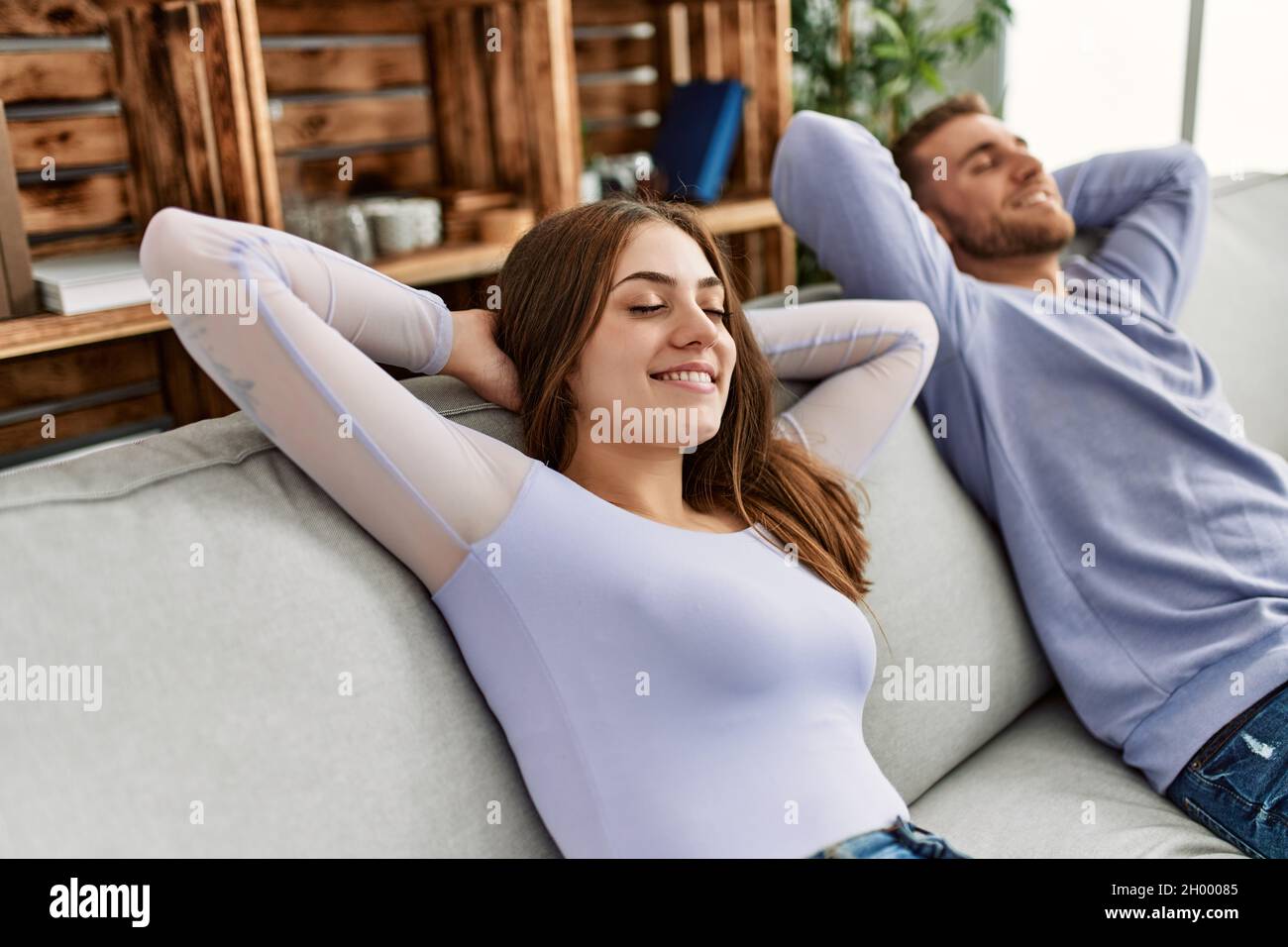 Young caucasian couple resting with hands on head sitting on the sofa ...
