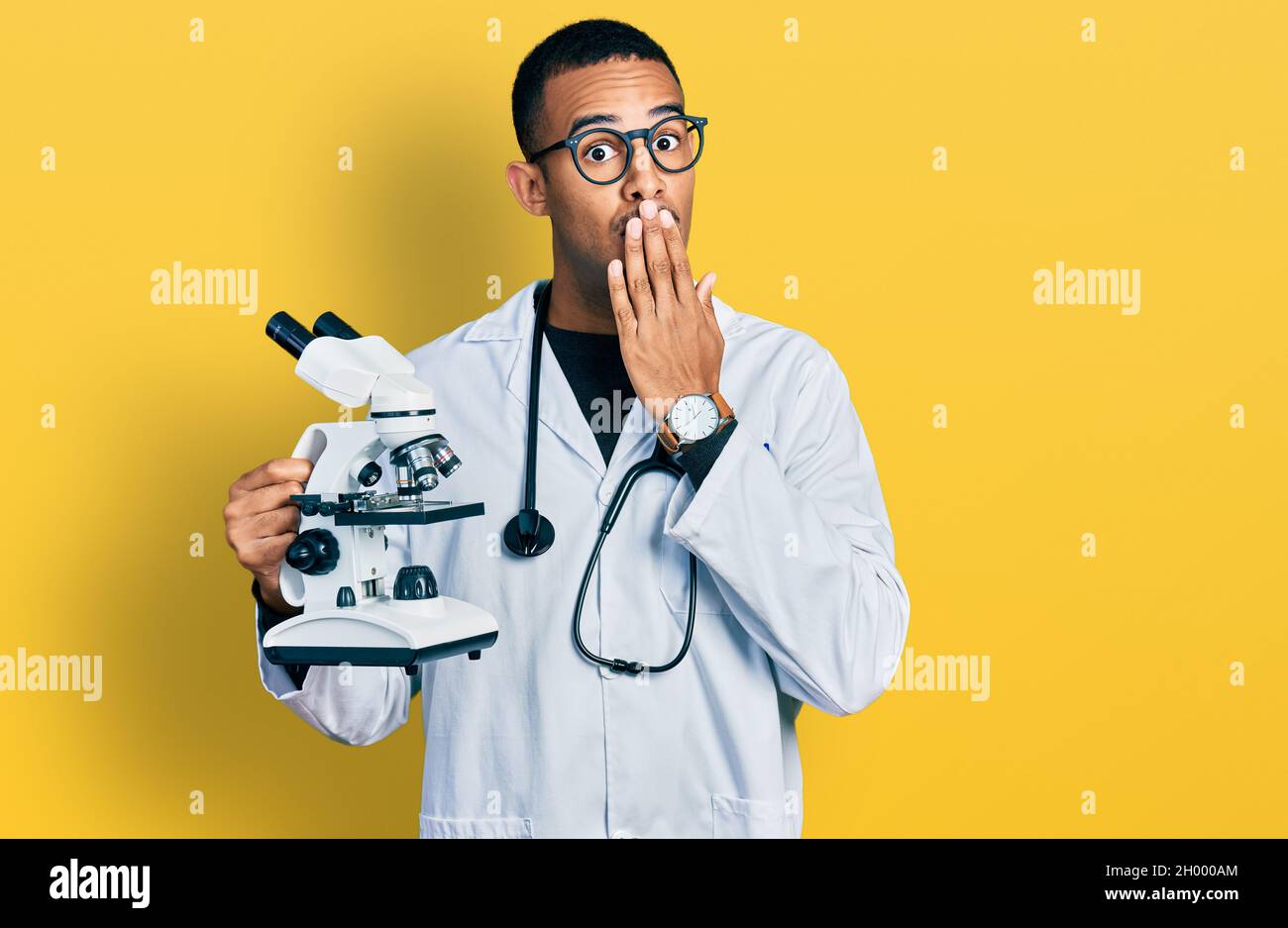 Young african american man wearing scientist uniform holding microscope ...
