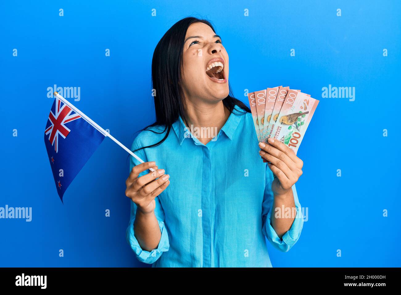 Young latin woman holding new zealand flag and dollars angry and mad ...