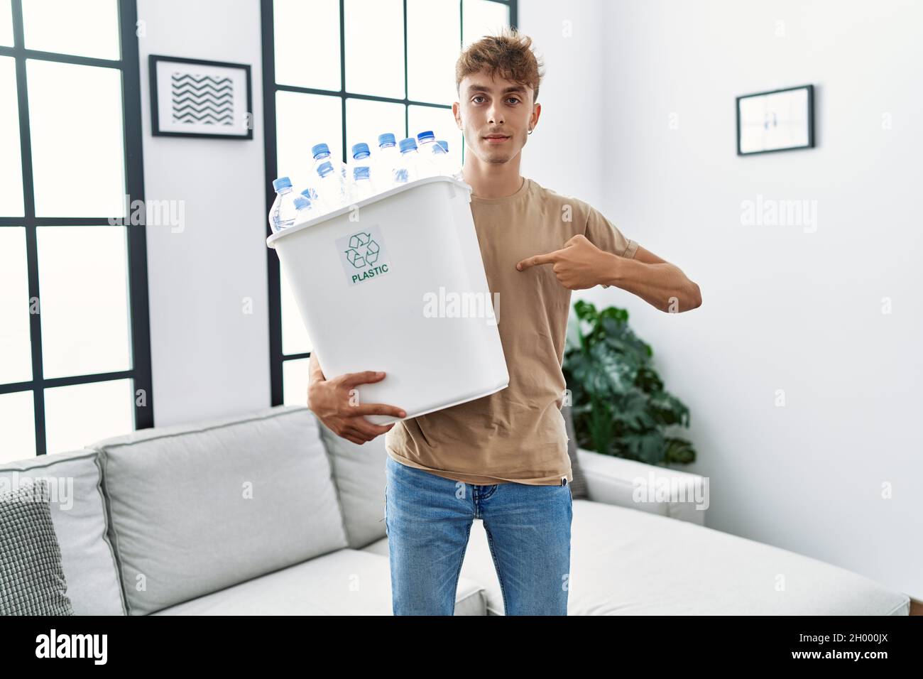 Young caucasian man holding wastebasket with recycling plastic bottles ...