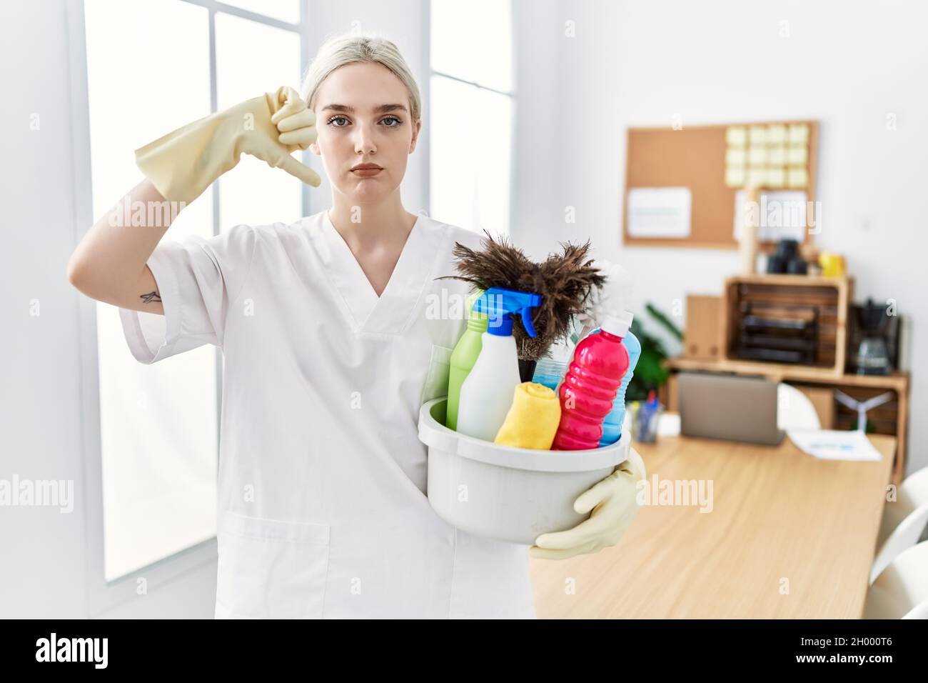 Young caucasian woman wearing cleaner uniform holding cleaning products ...