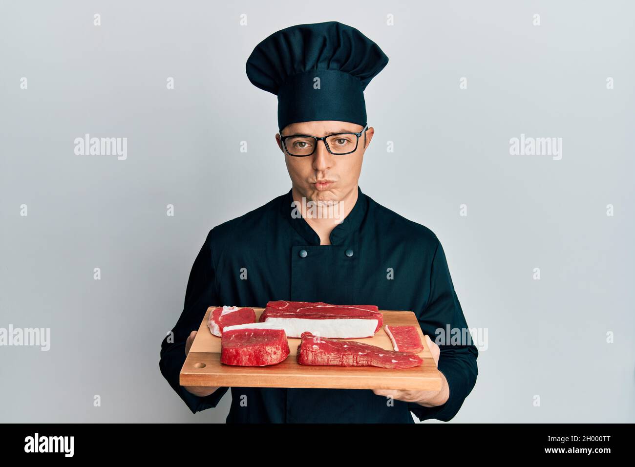 Handsome young man wearing chef uniform holding board with raw meat ...