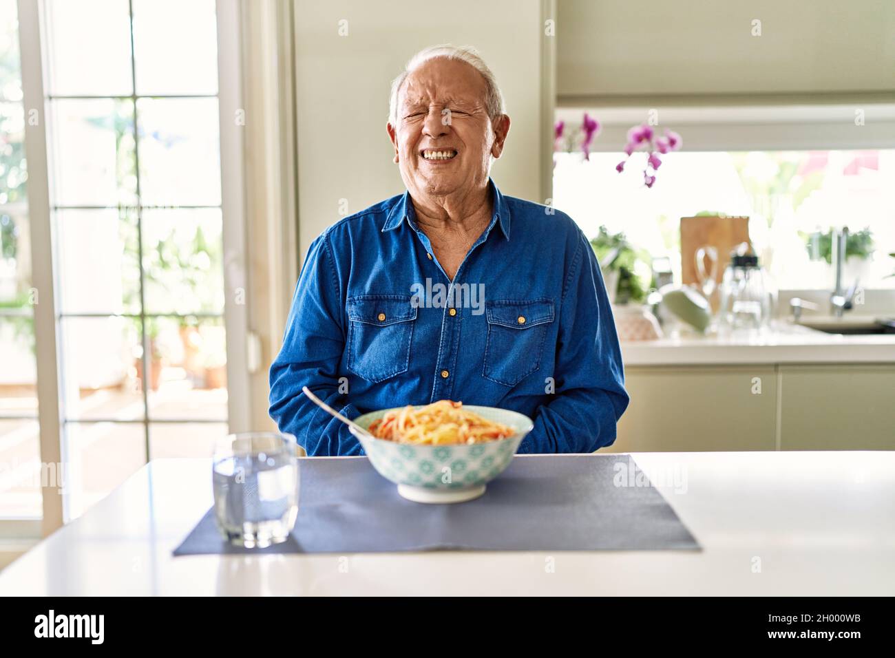 Senior man with grey hair eating pasta spaghetti at home with hand on ...
