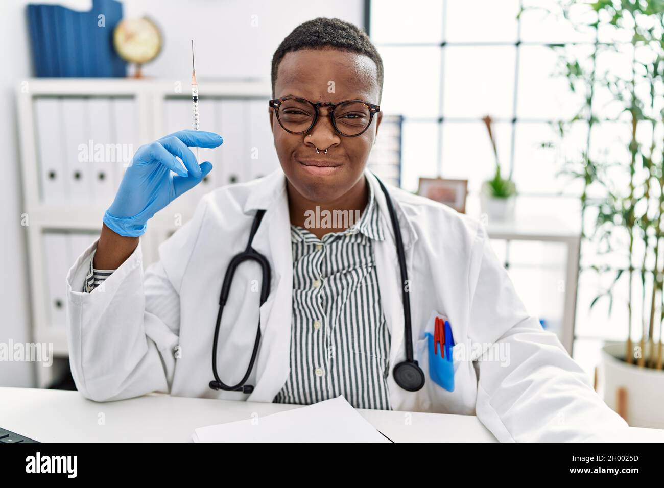 Young african doctor man holding syringe at the hospital puffing cheeks ...