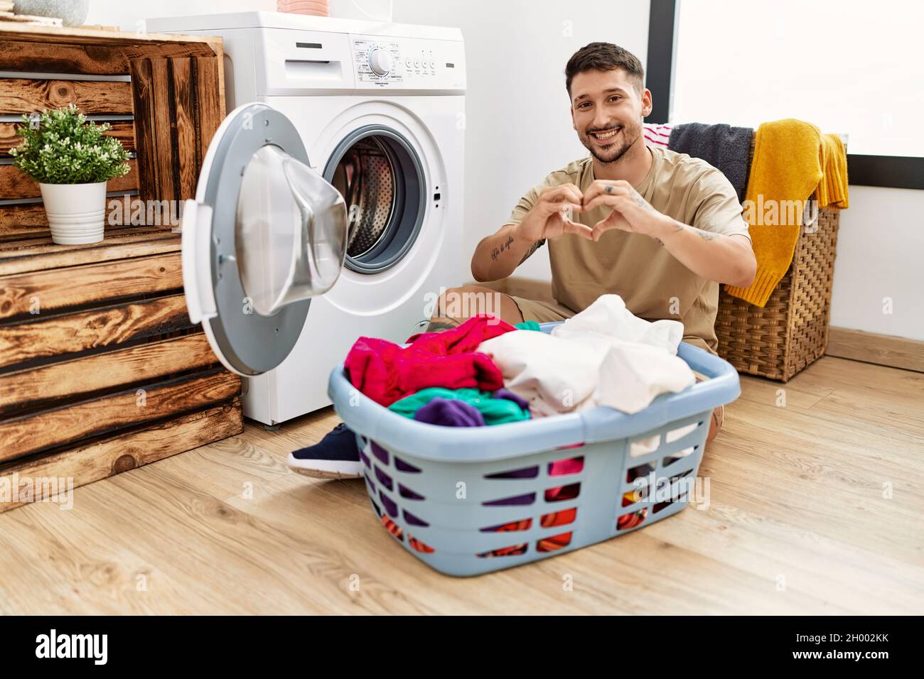 Young handsome man putting dirty laundry into washing machine smiling ...