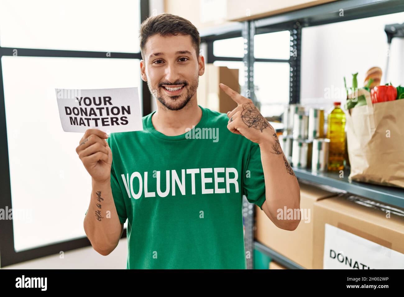 Young volunteer man holding your donation matters banner pointing finger to one self smiling ...