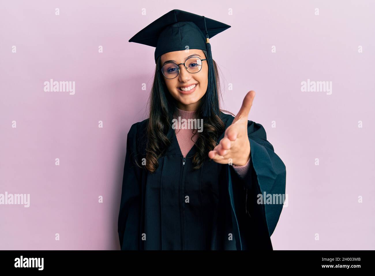 Young hispanic woman wearing graduation cap and ceremony robe smiling ...