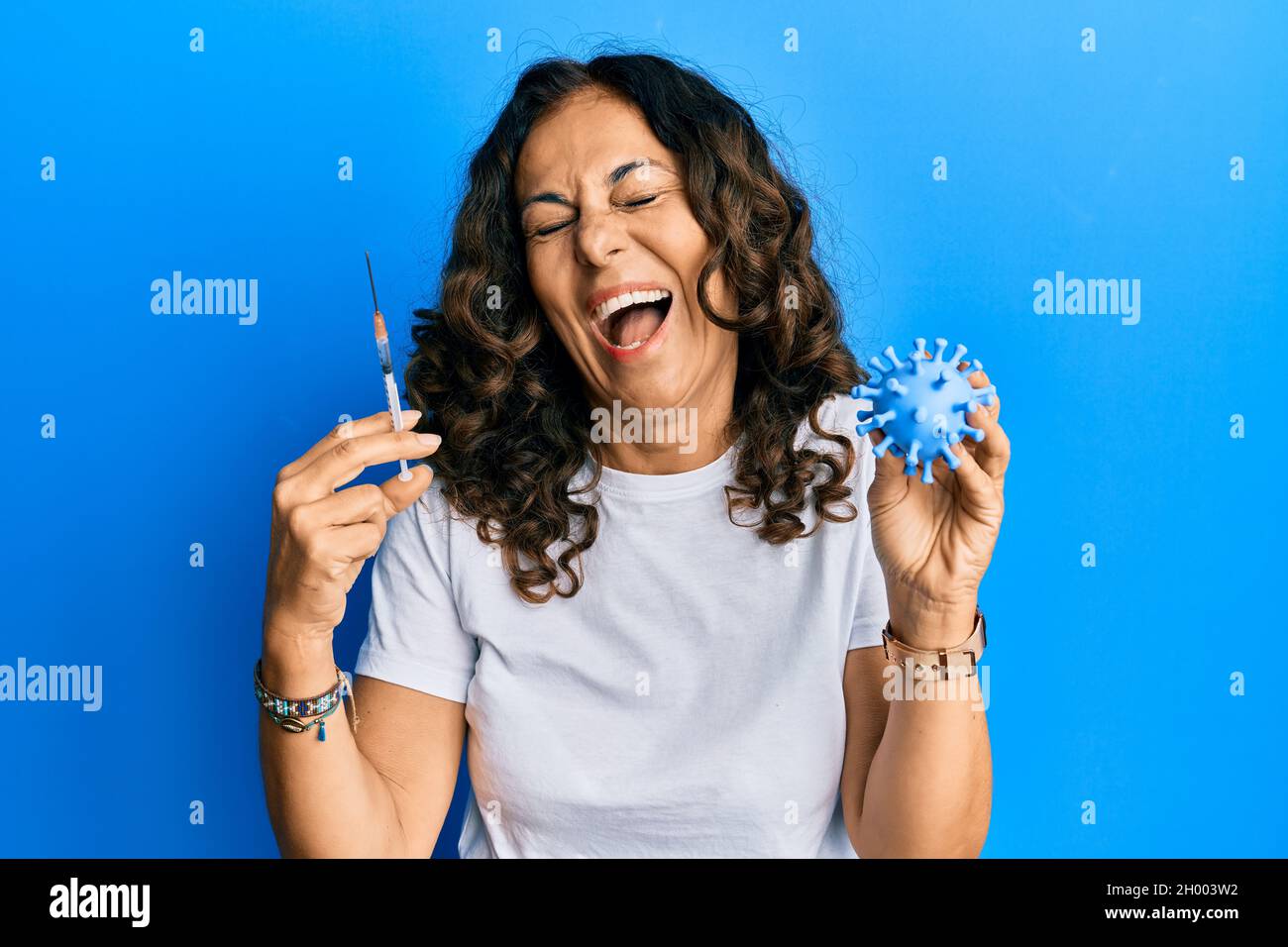 Middle age hispanic woman holding virus toy and syringe smiling and ...