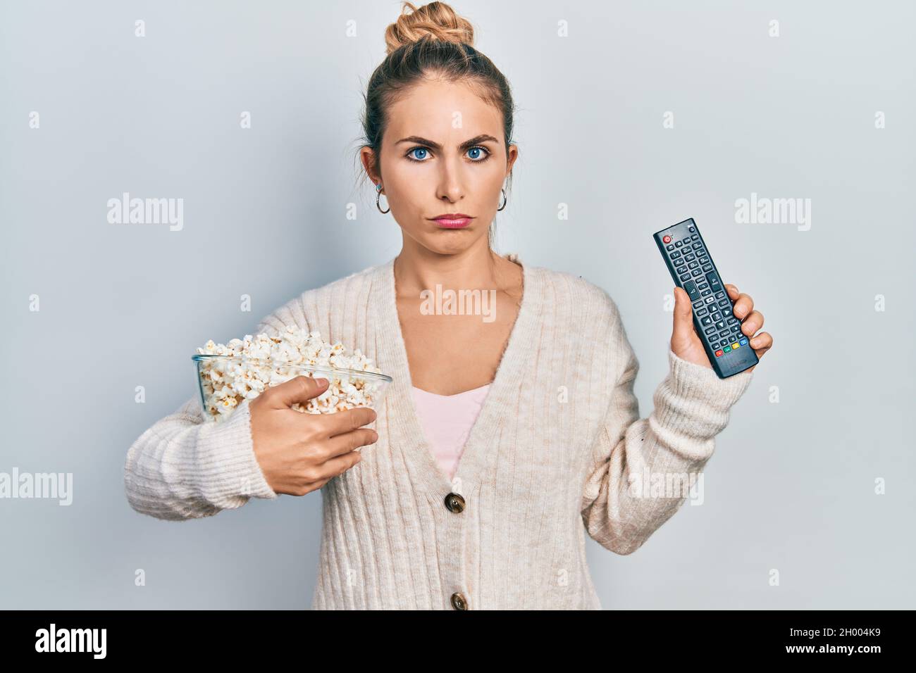 Young caucasian woman eating popcorn using tv control depressed and ...