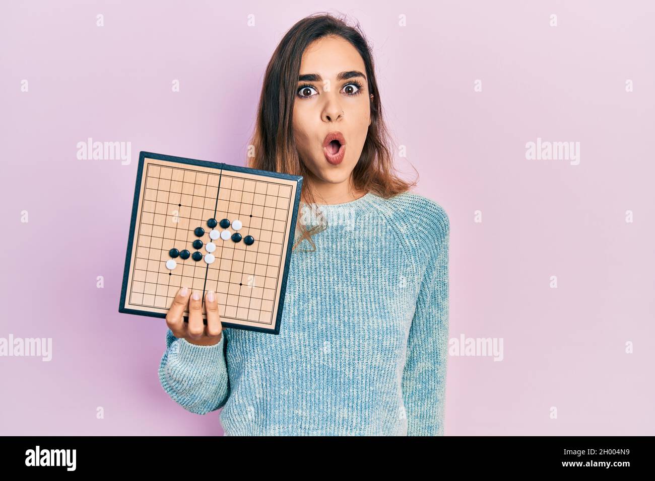 Young hispanic girl holding asian go game board scared and amazed with ...