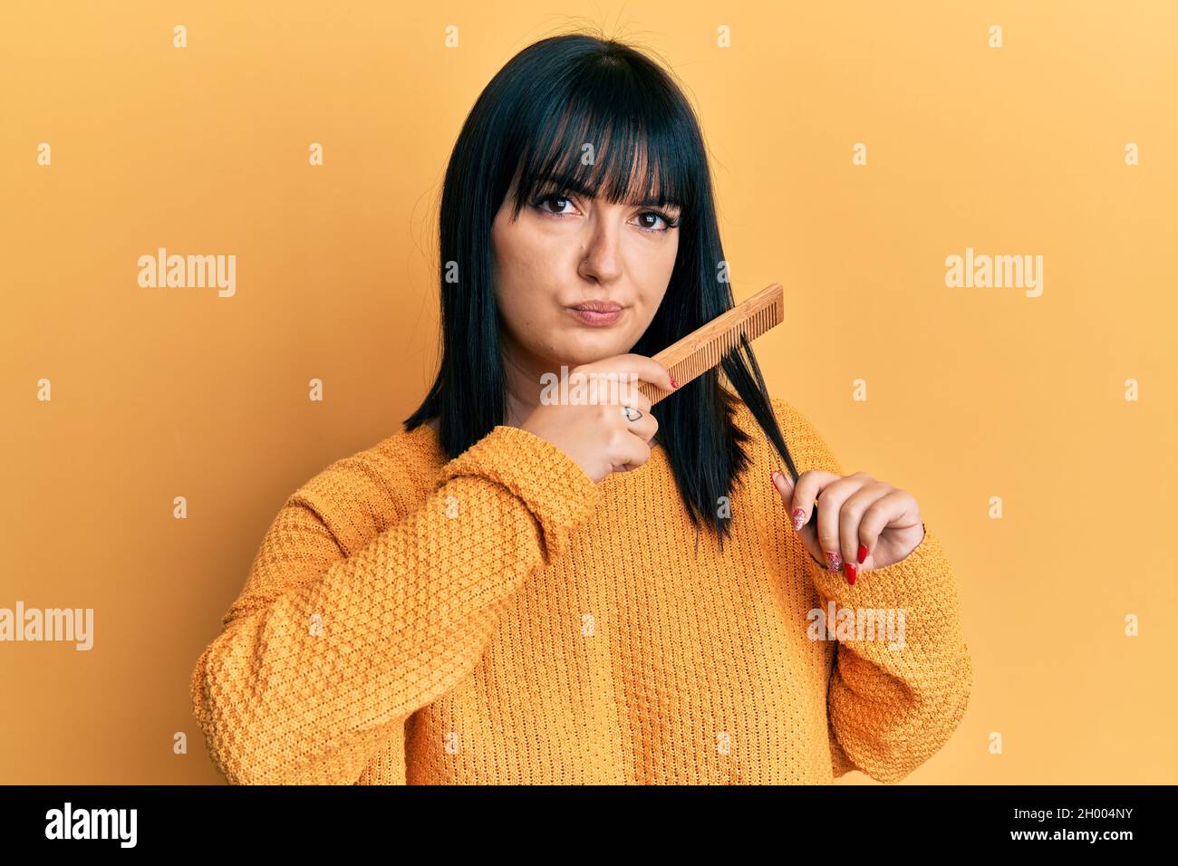 Young hispanic woman styling hair using comb skeptic and nervous ...