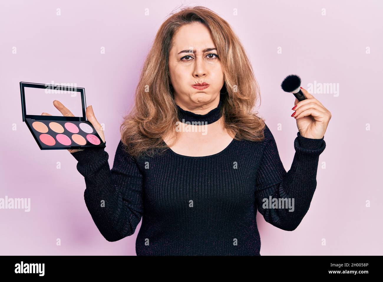 Middle age caucasian woman holding makeup brush and blush puffing ...