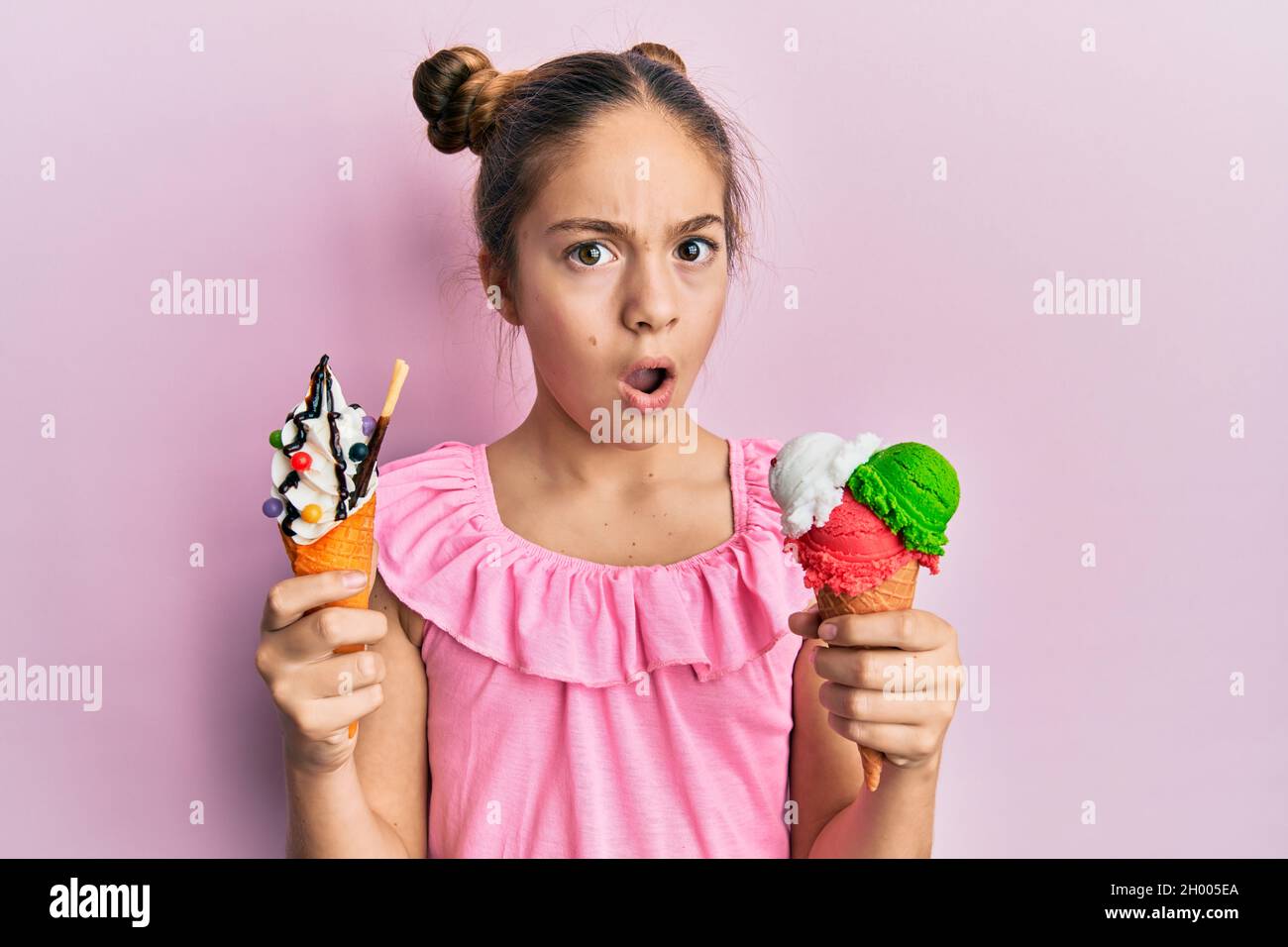 Beautiful brunette little girl eating ice cream cones in shock face ...