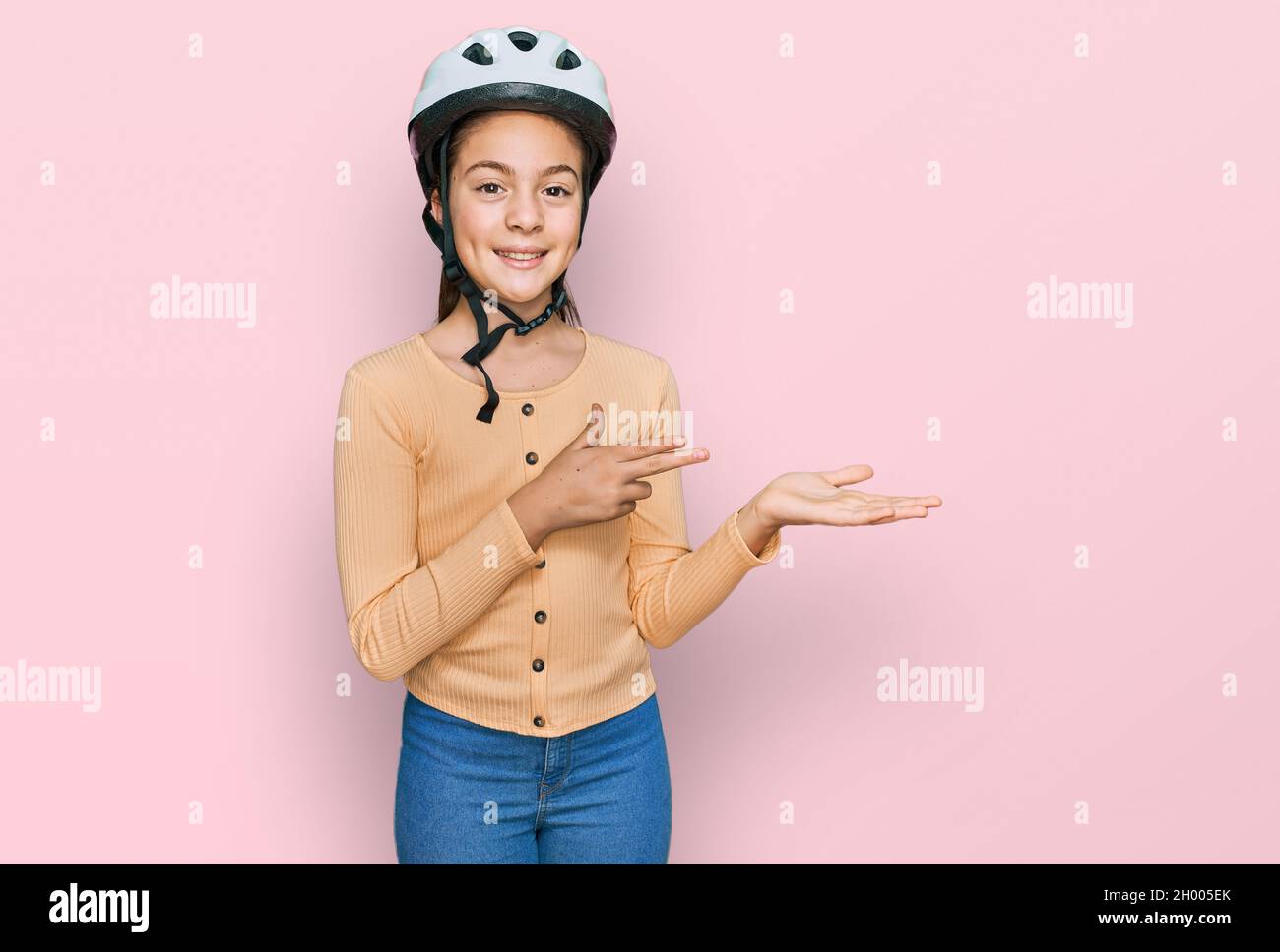 Beautiful brunette little girl wearing bike helmet amazed and smiling to the camera while ...