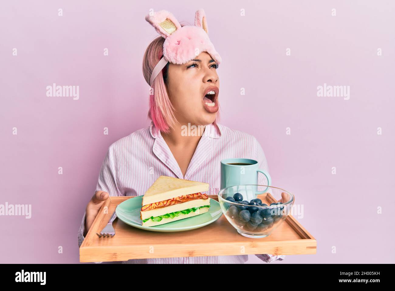 Hispanic woman with pink hair wearing pajama holding healthy breakfast ...