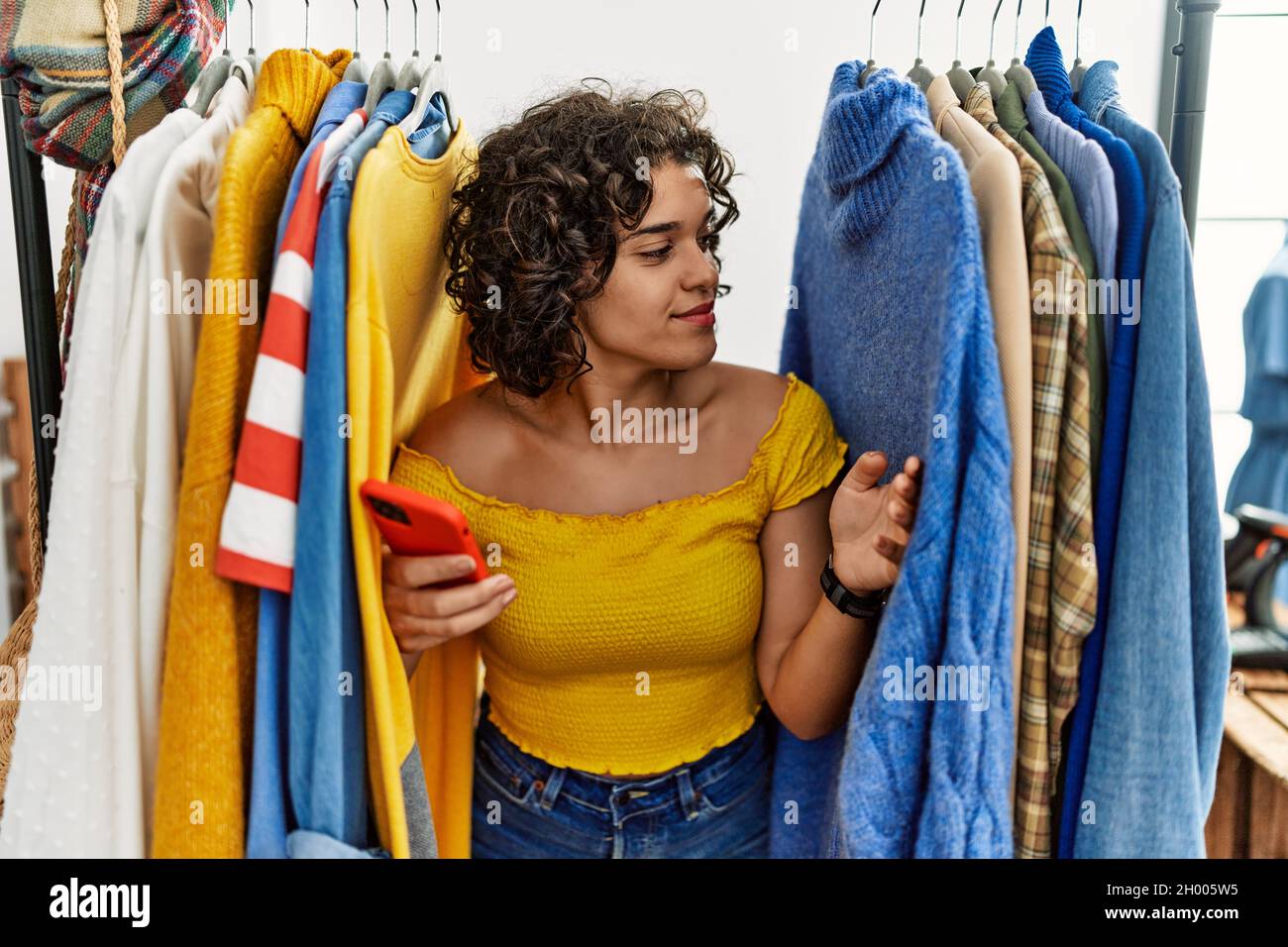 Young hispanic woman searching clothes on clothing rack using ...
