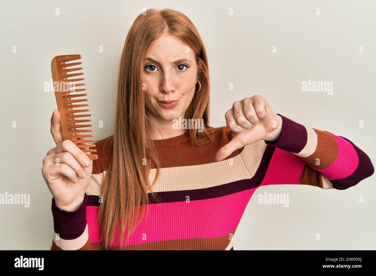 Young irish woman styling hair using comb with angry face, negative ...