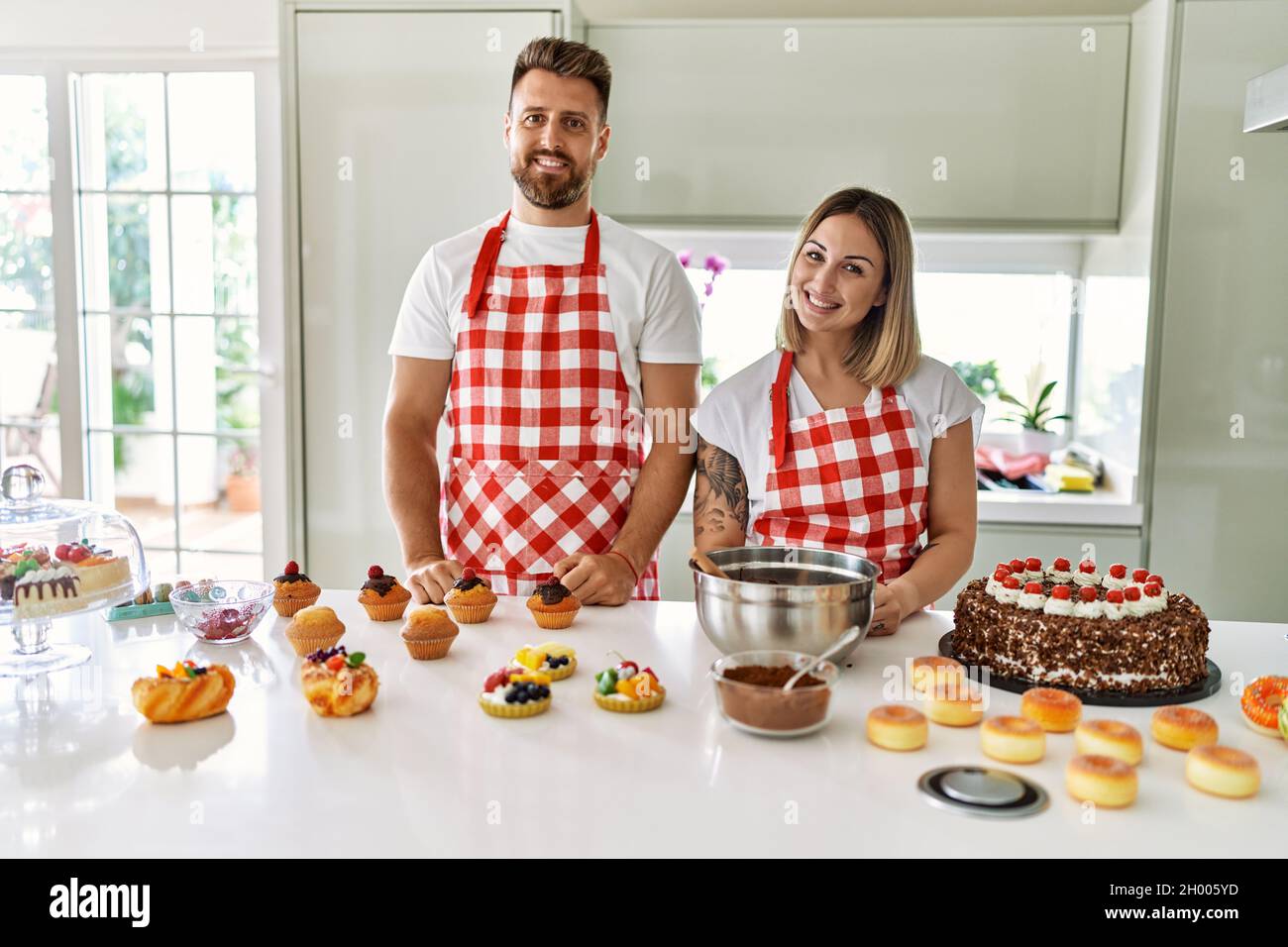 Young couple cooking pastries at the kitchen looking positive and happy ...