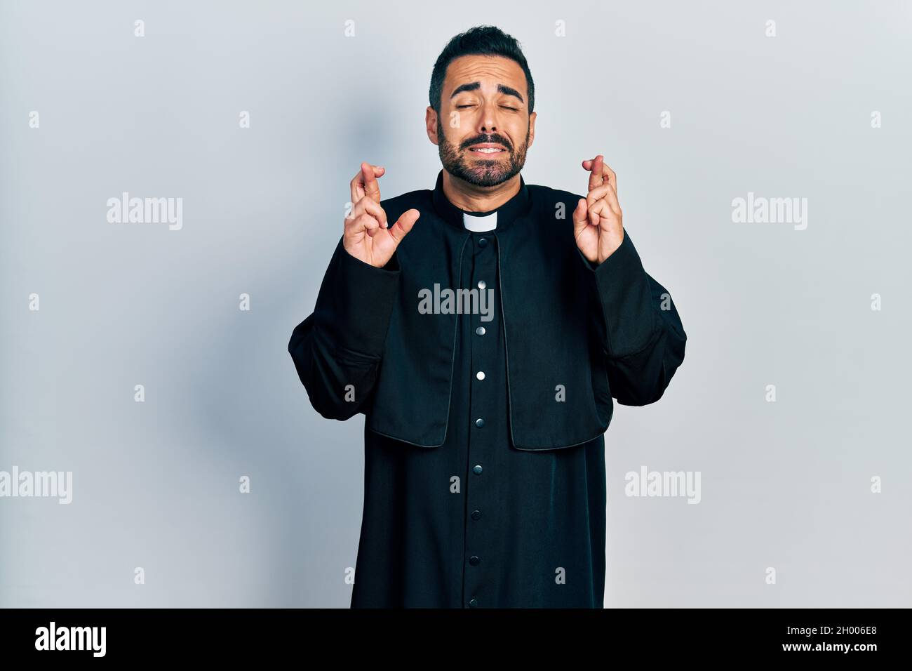 Handsome hispanic man with beard wearing catholic priest robe gesturing ...