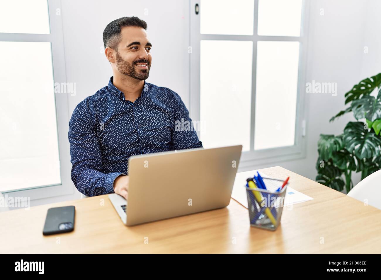 Young hispanic man with beard working at the office with laptop looking ...