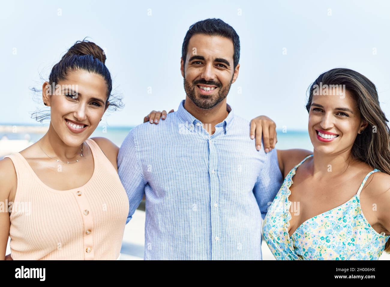 Three young hispanic friends smiling happy and hugging at the beach ...