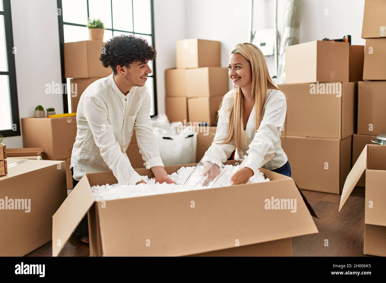 Young beautiful couple smiling happy unboxing cardboard box at new home ...
