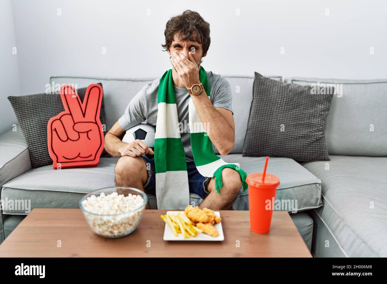 Young hispanic man football hooligan cheering game at home smelling ...
