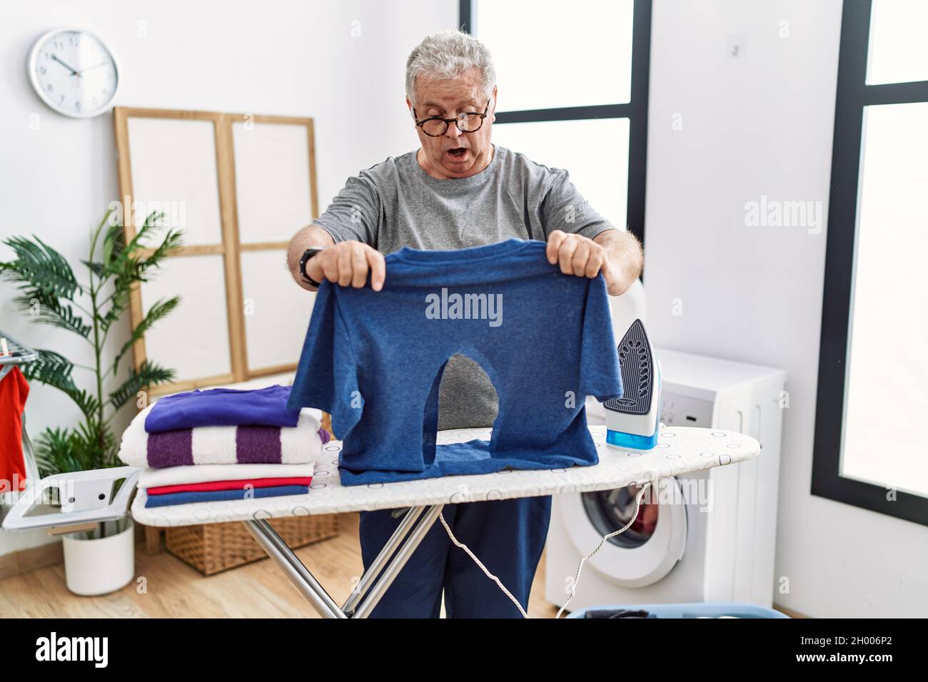 Senior caucasian man ironing holding burned iron shirt at laundry room ...