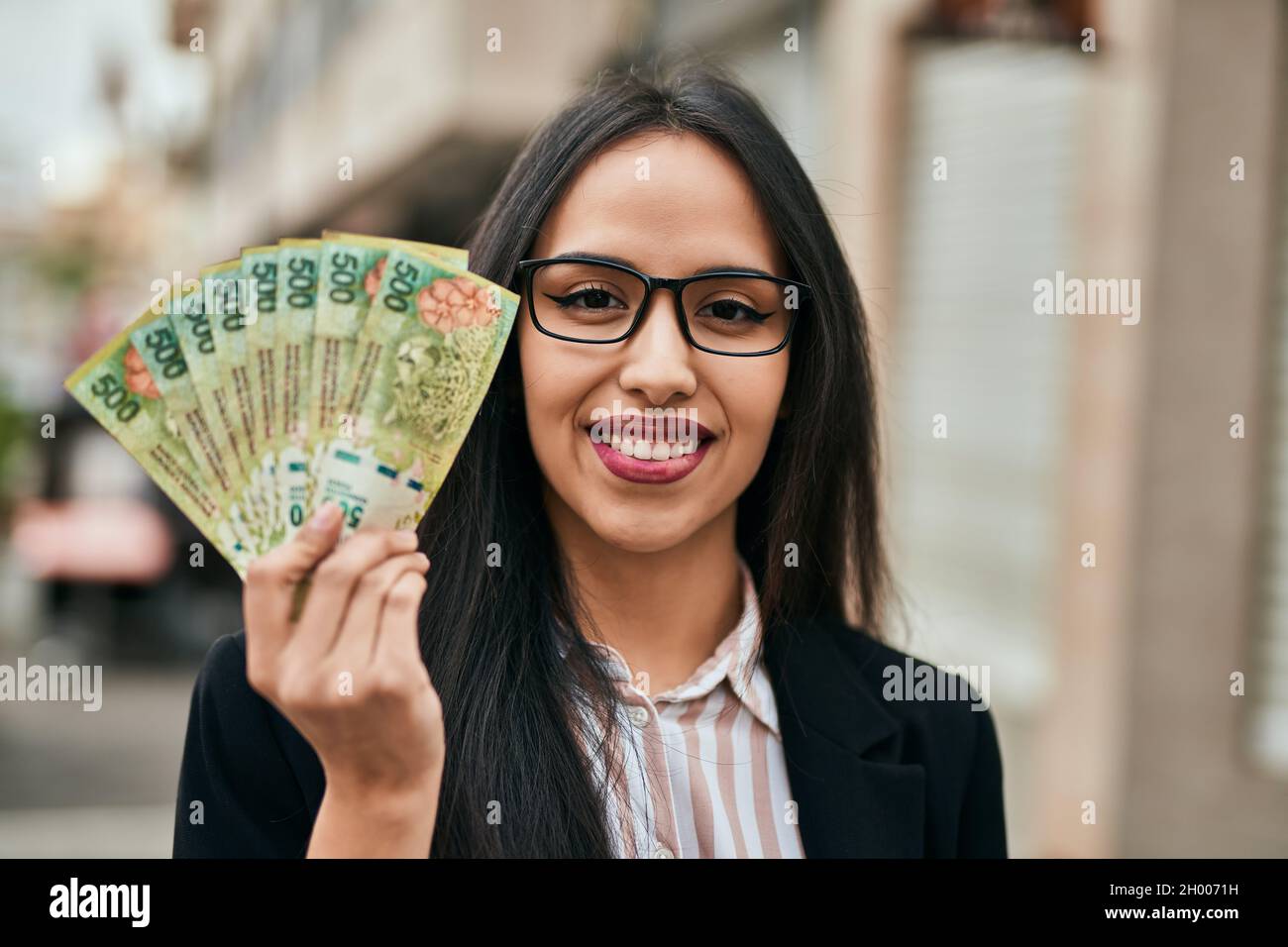 Young hispanic businesswoman holding argentina pesos banknotes at the ...