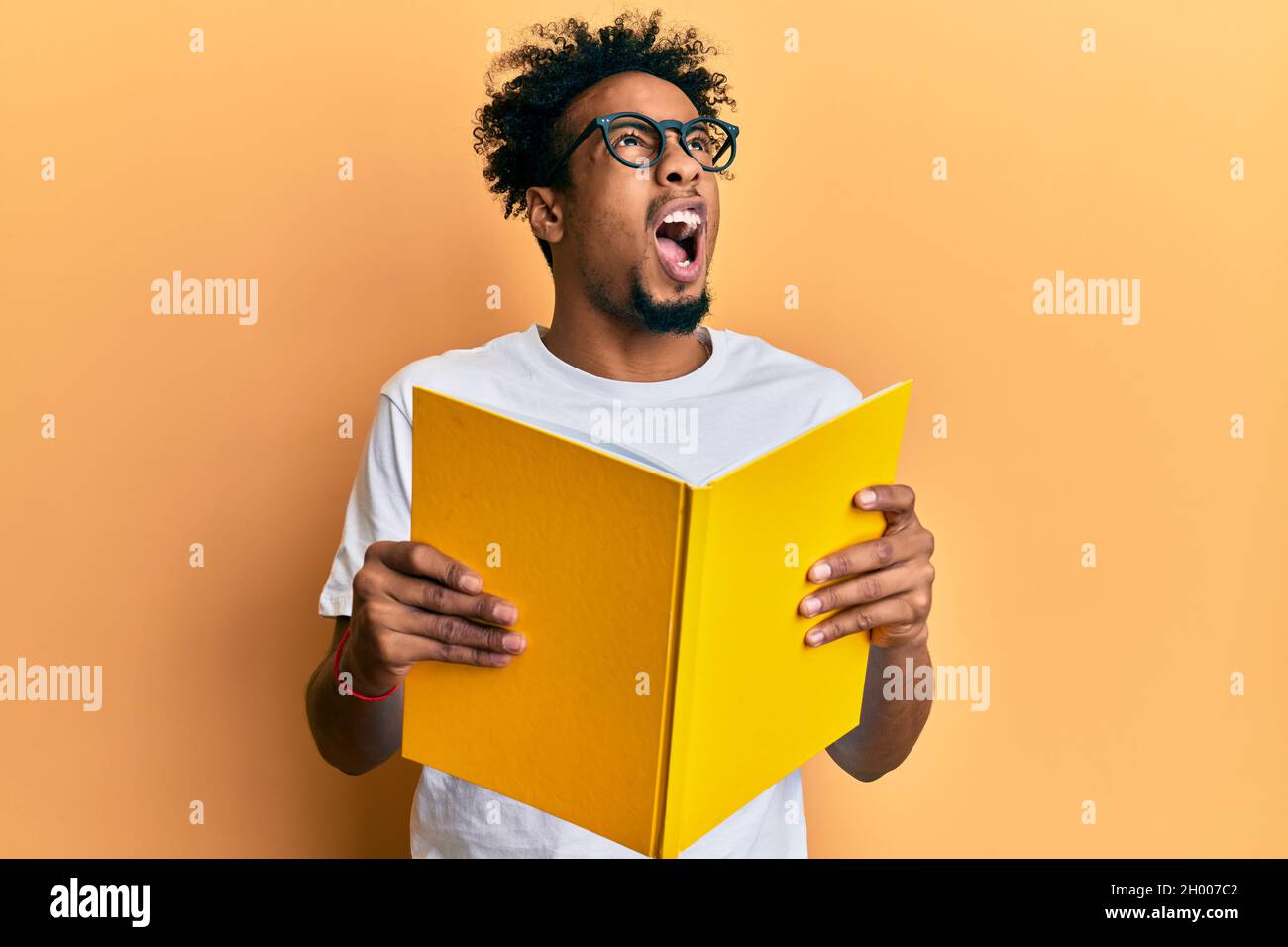 Young african american man with beard reading a book wearing glasses ...