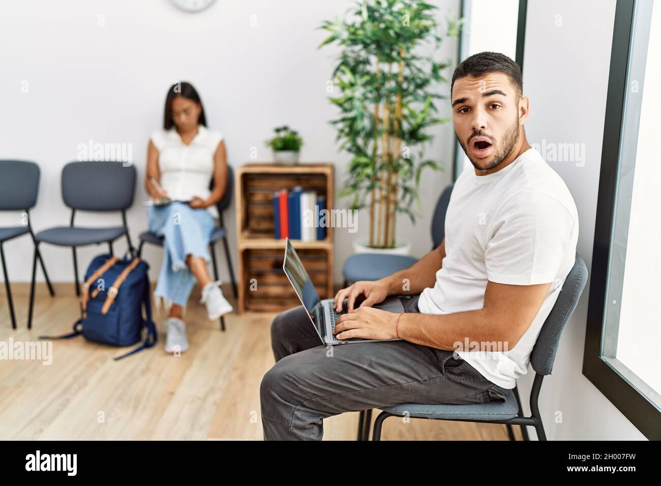 Young people sitting at waiting room working with laptop scared and ...