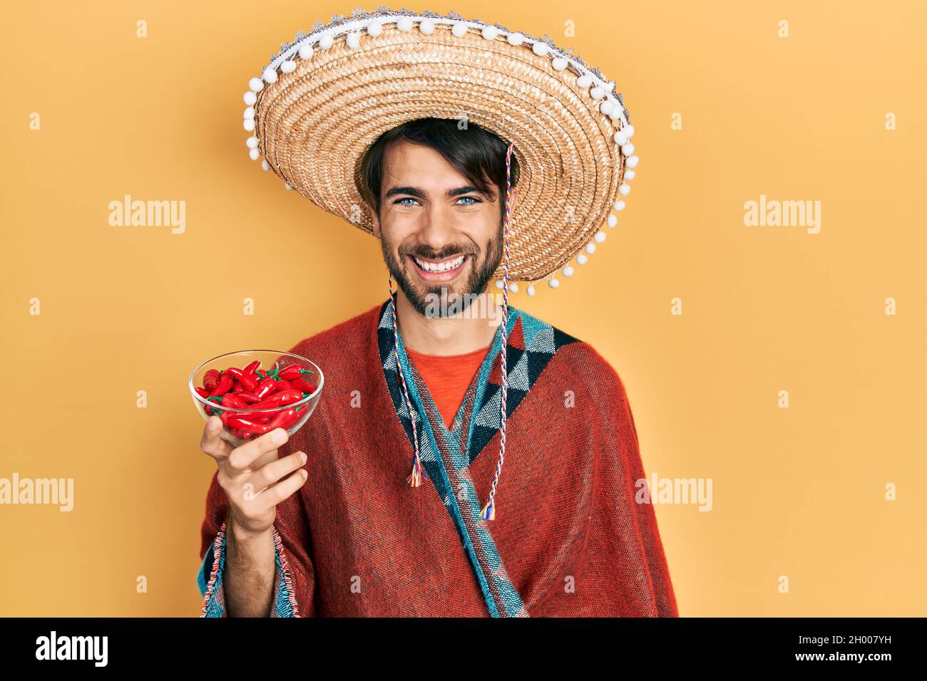 Young hispanic man wearing mexican hat holding chili looking positive ...