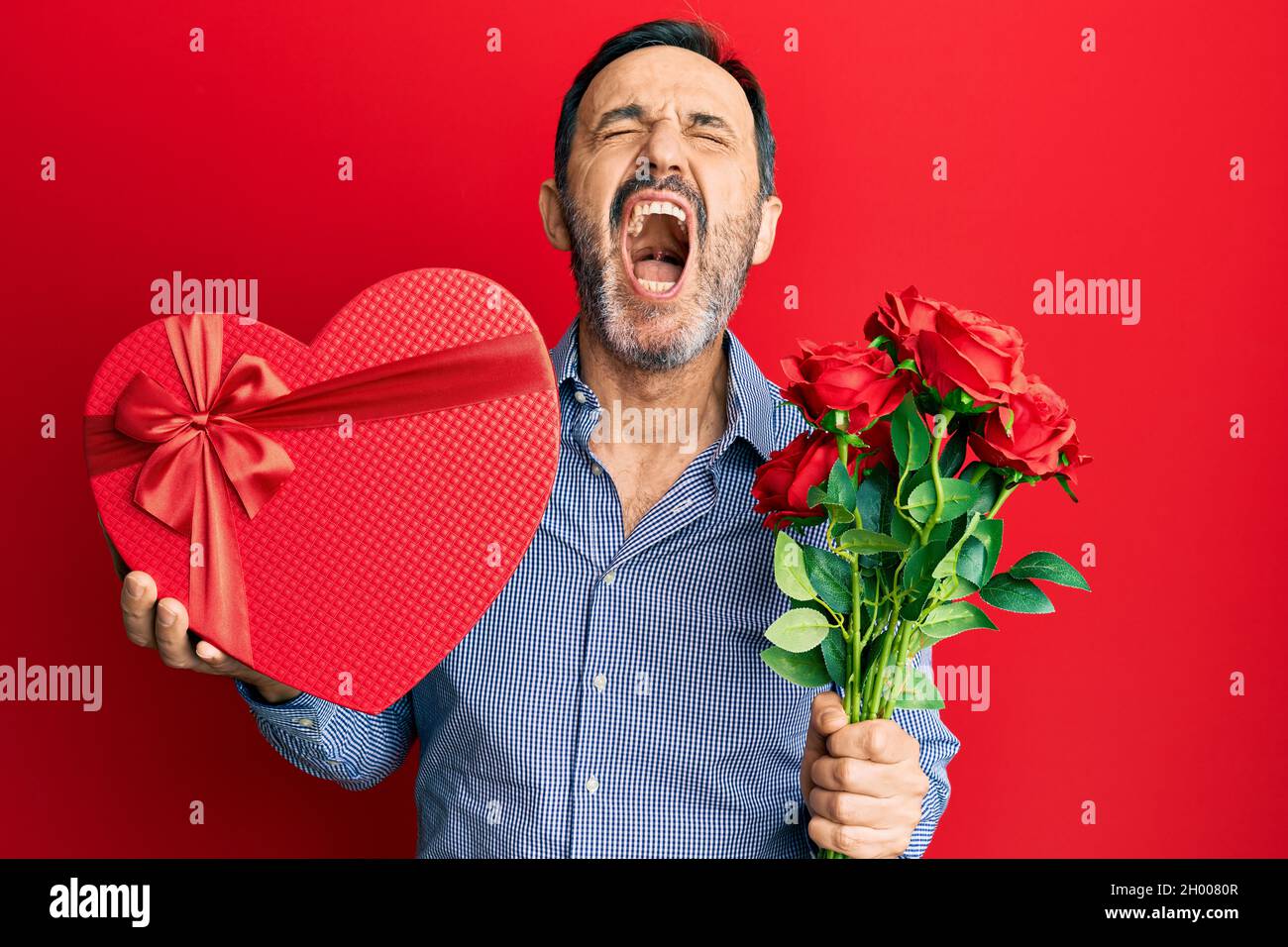 Middle age hispanic man holding valentine day gift and flowers angry ...