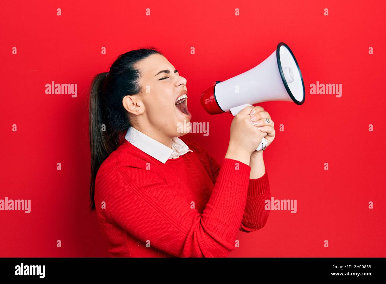 Young brunette woman screaming through megaphone over isolated red ...