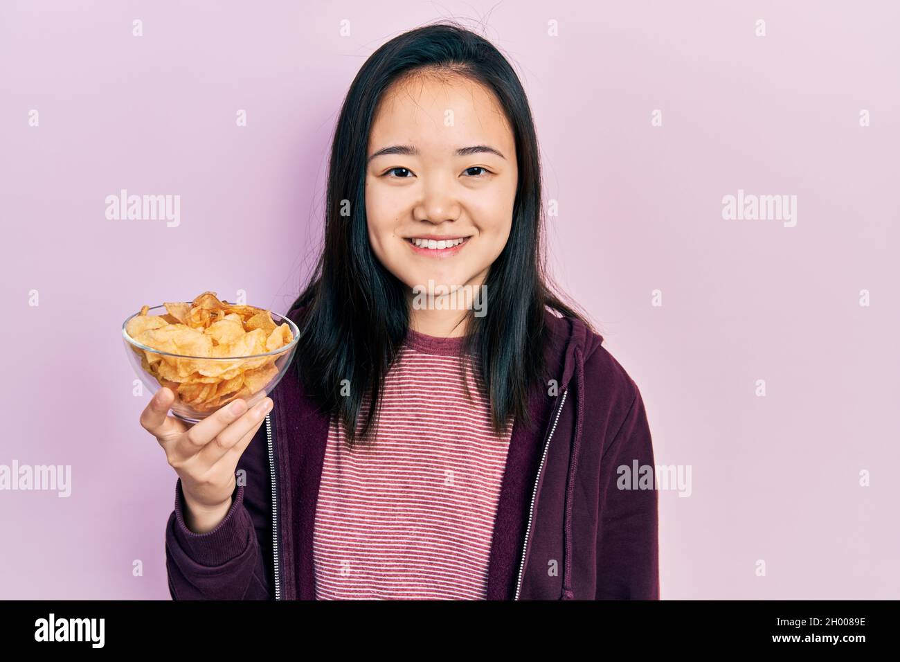 Young chinese girl holding potato chip looking positive and happy ...