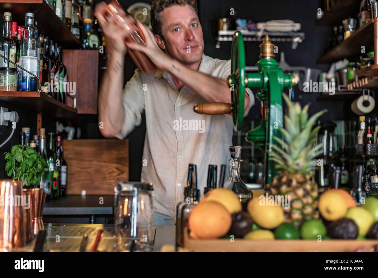 View of a professional bartender shaking a cocktail behind the counter of a tiny small bar ...